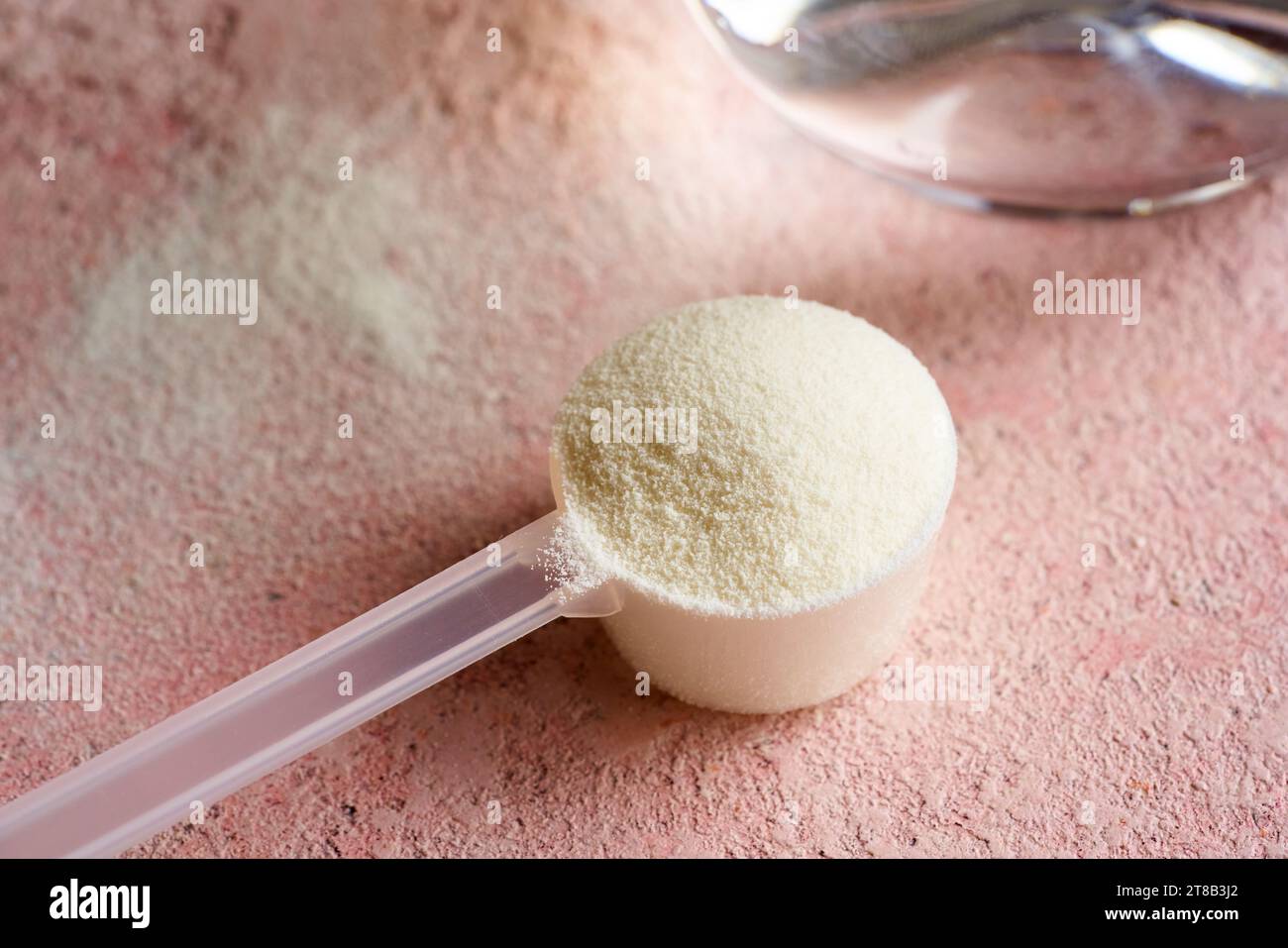 Collagen powder in a plastic measuring cup on pink background next to a ...