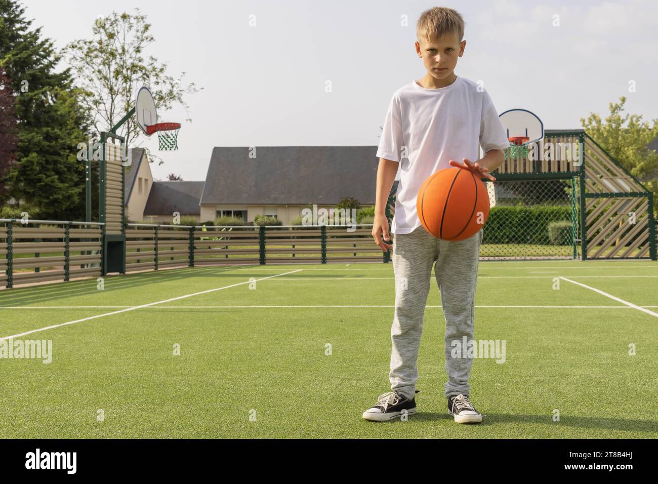 a boy in a white t-shirt and gray pants stands on a basketball court ...