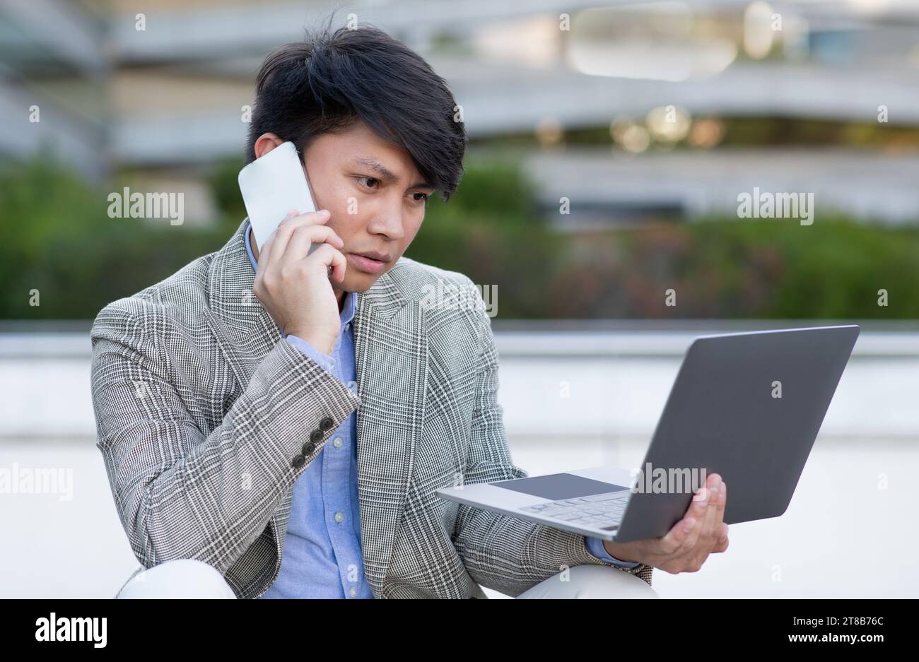 Displeased Korean manager man using laptop talking with phone outdoors ...