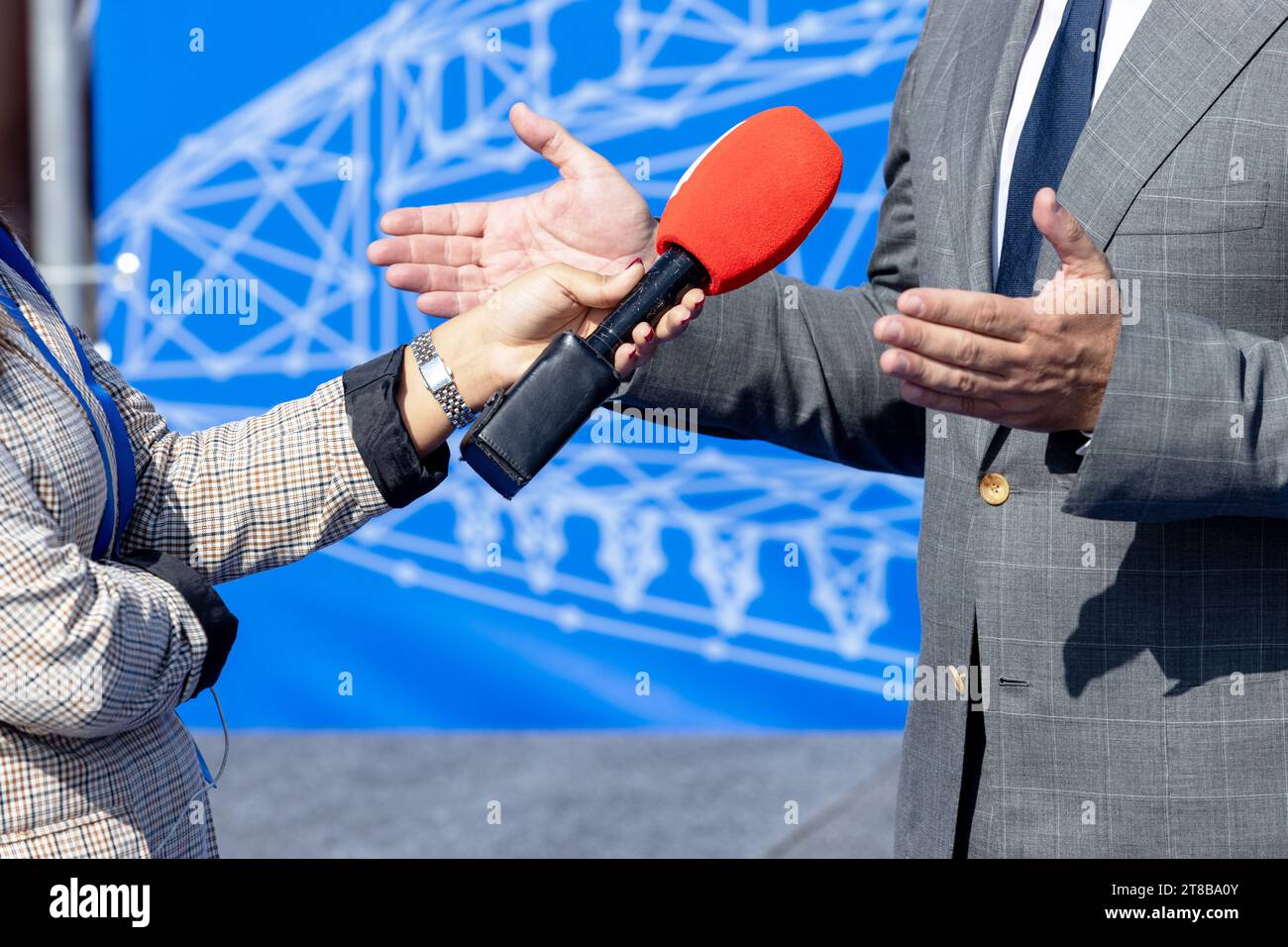 Female news reporter holding microphone making media interview with male unrecognizable person ...