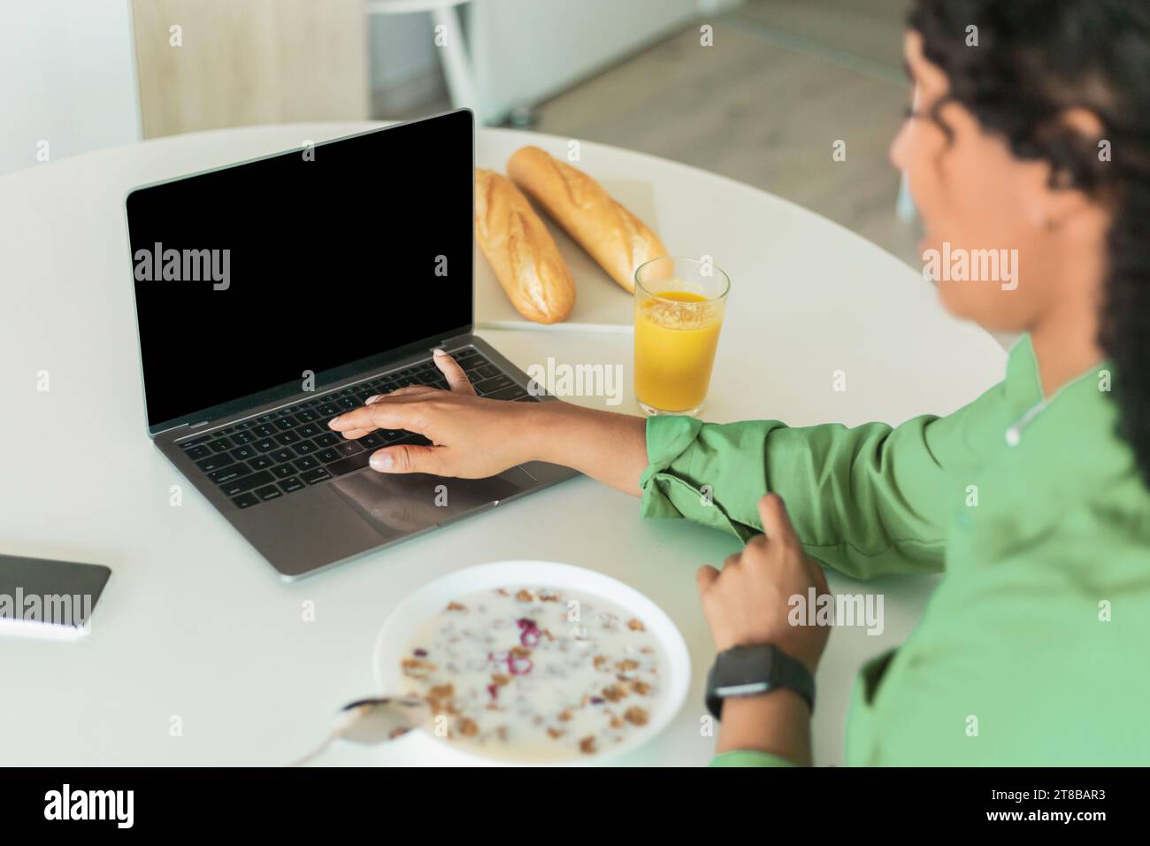 black woman using laptop with blank screen having breakfast indoor ...