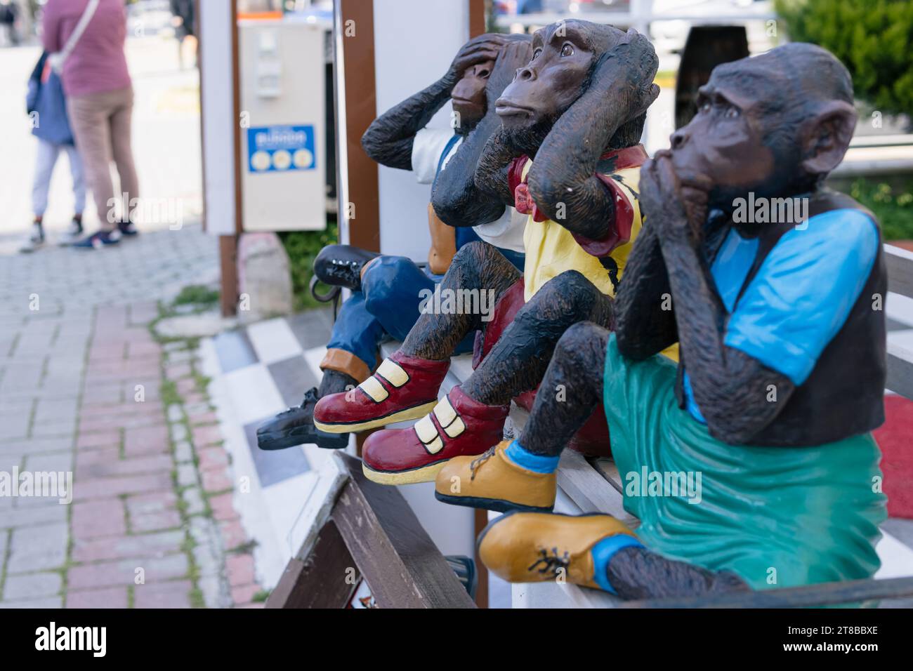 figures of three monkeys in clothes sitting on a bench on the street ...