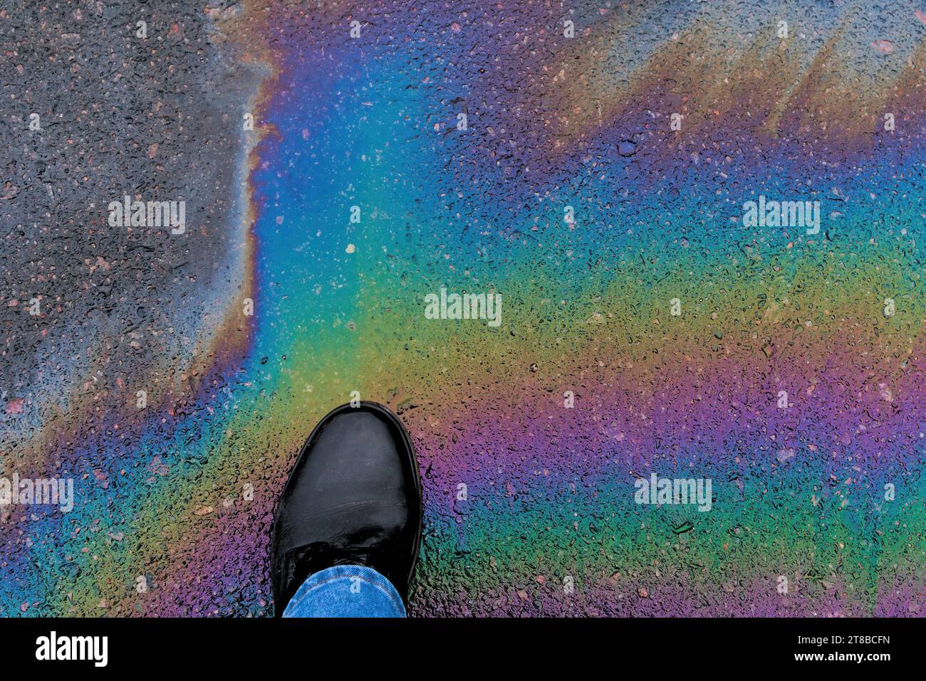 A man's foot steps on a rainbow stain of gasoline on the asphalt ...