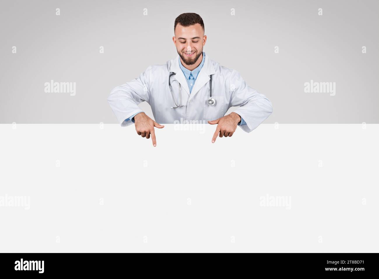 Male doc pointing at white placard, grey background Stock Photo - Alamy