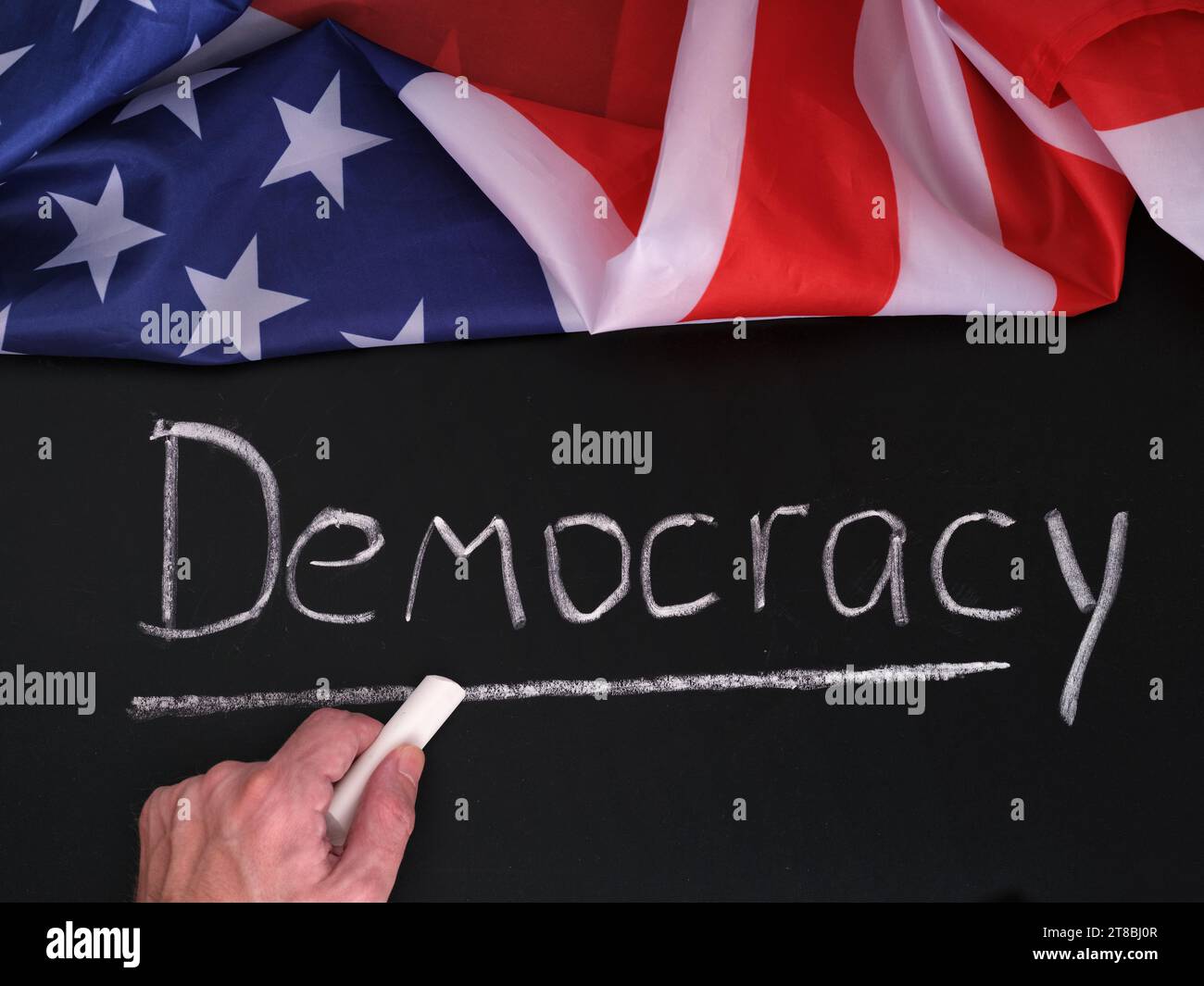 The flag of the USA lying on a chalkboard with the word Democracy being ...