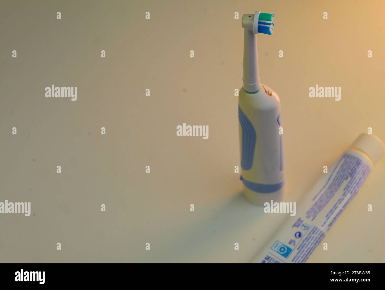 A photo of a tall, white electric toothbrush beside a squeezed tube of ...