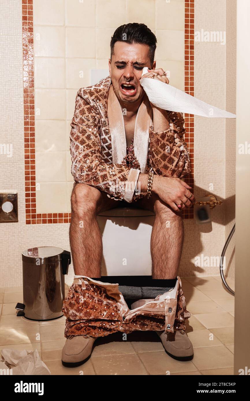 Rich man, dressed in a radiant golden suit, sits on a toilet and cries ...