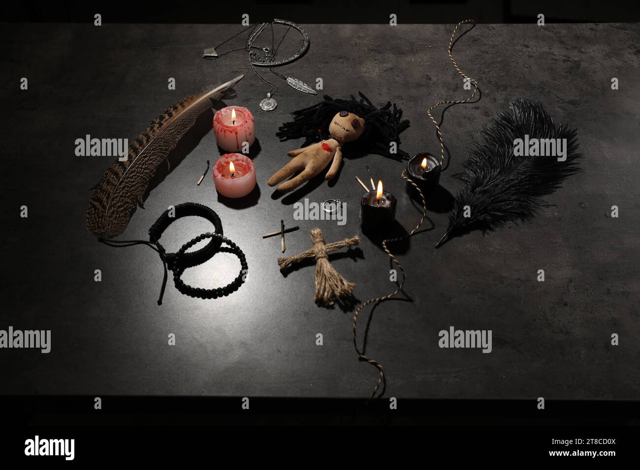 Female voodoo doll with pin in heart and ceremonial items on grey table ...