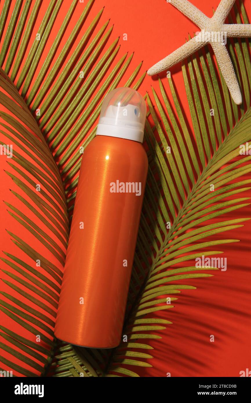 Sunscreen, starfish and tropical leaves on coral background, flat lay ...