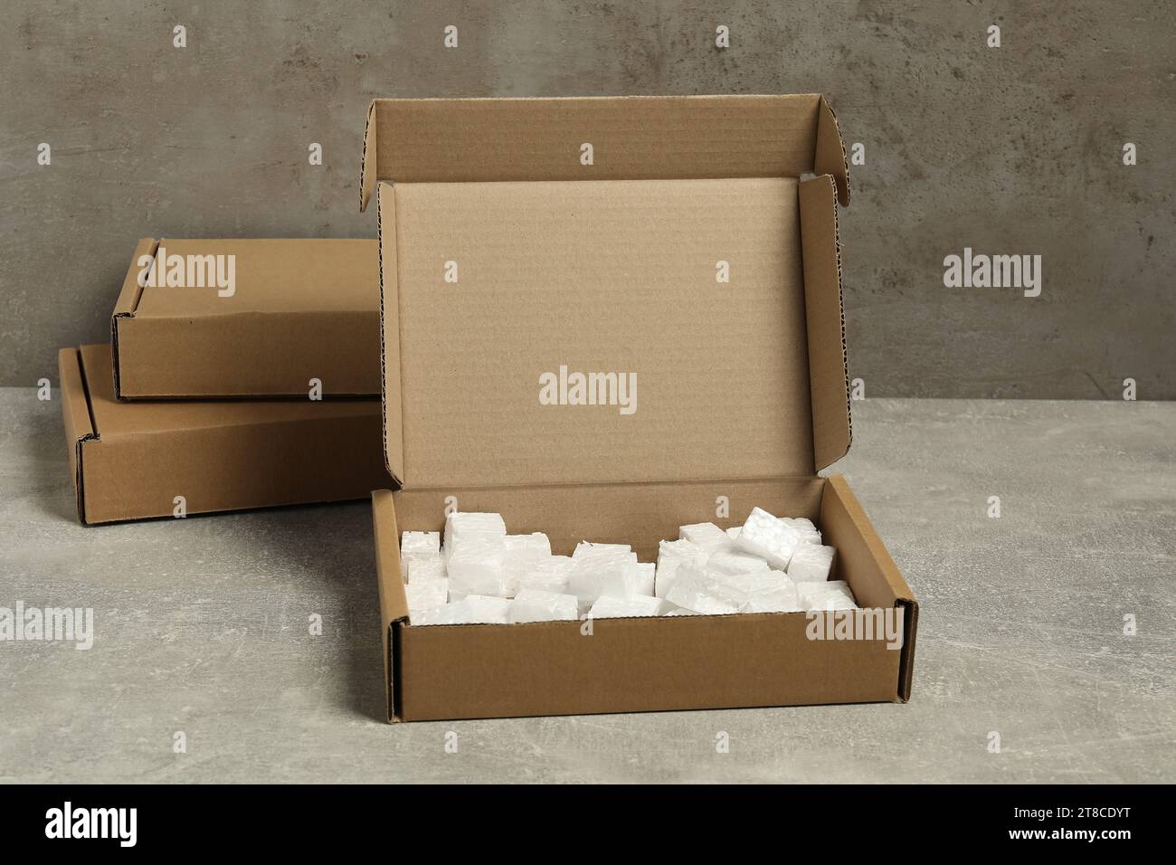 Cardboard boxes with pieces of polystyrene foam on grey textured table ...