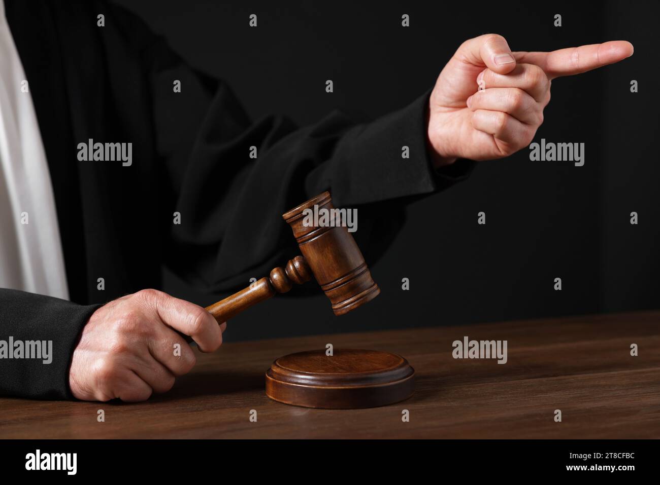 Judge with gavel pointing at wooden table against black background ...