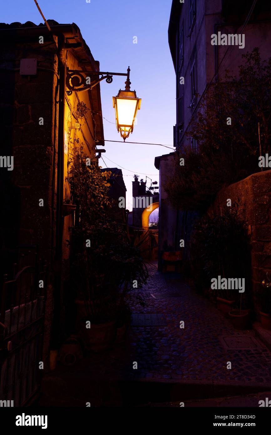 Street lamp lights a narrow cobbled street at dusk in the historic ...