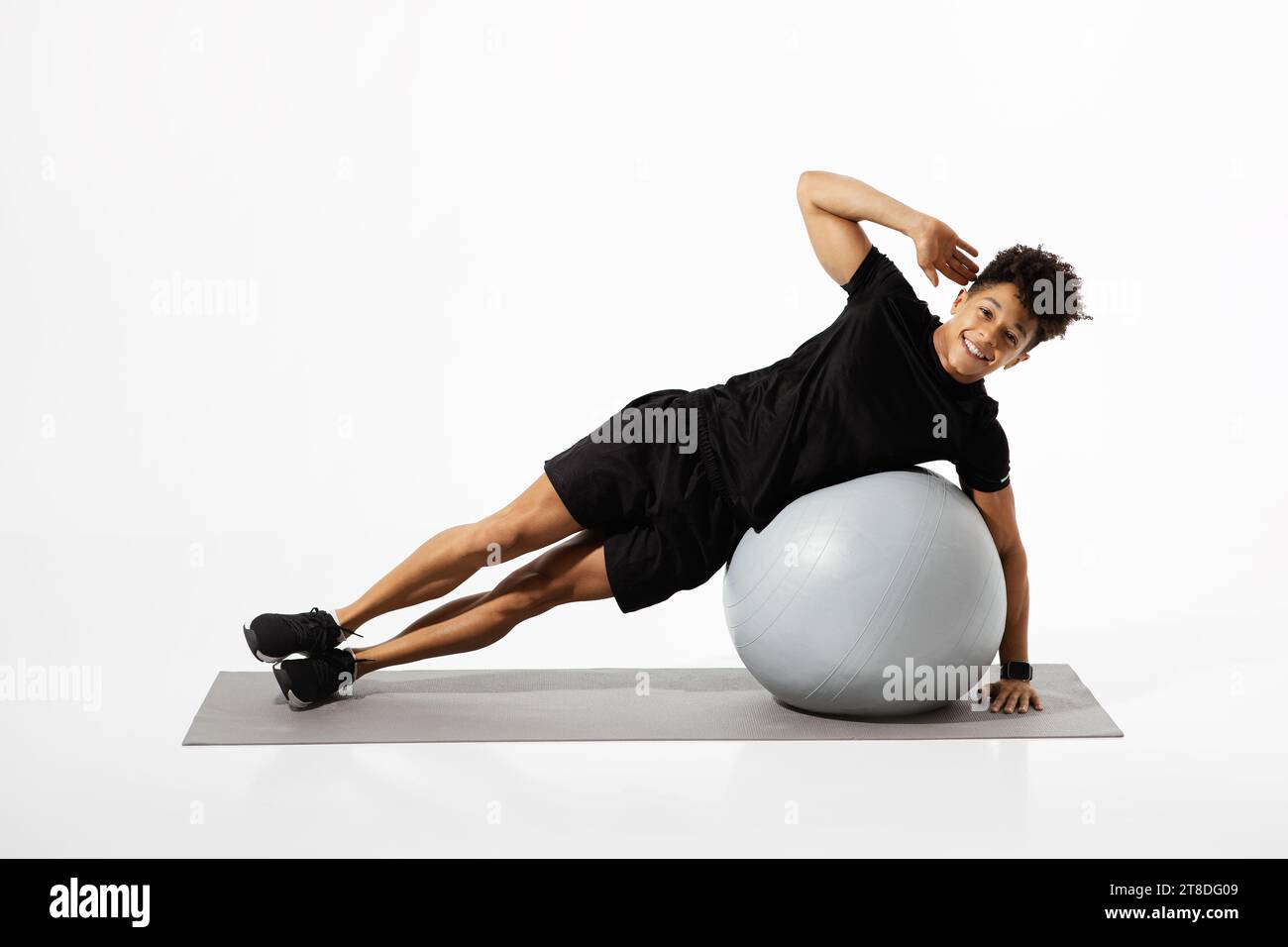 man performs side plank exercise on balance ball, white background ...