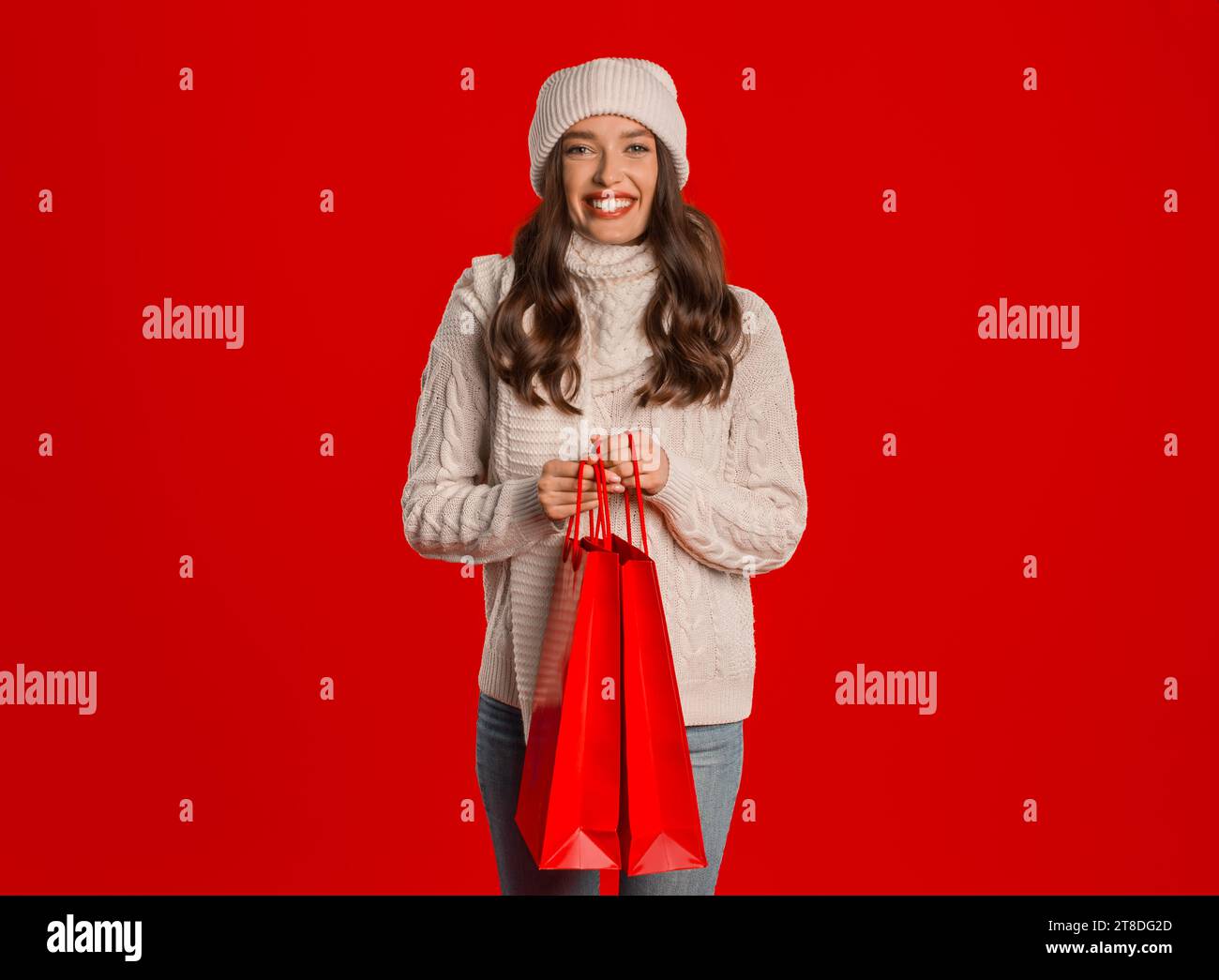Cheerful customer woman holding bags of Xmas purchases, red background ...