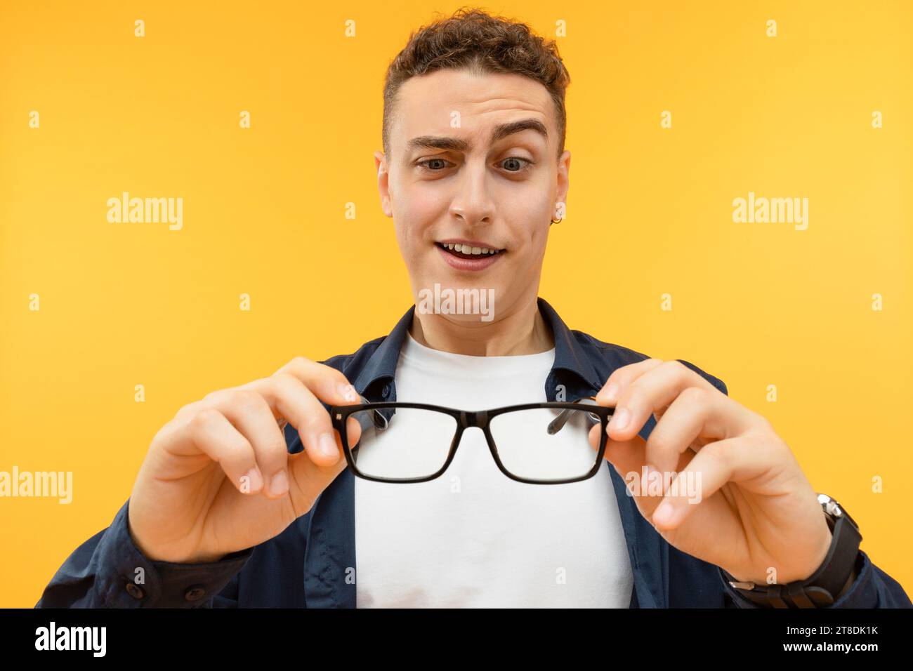 Surprised young man put on his eyeglasses, yellow background Stock ...