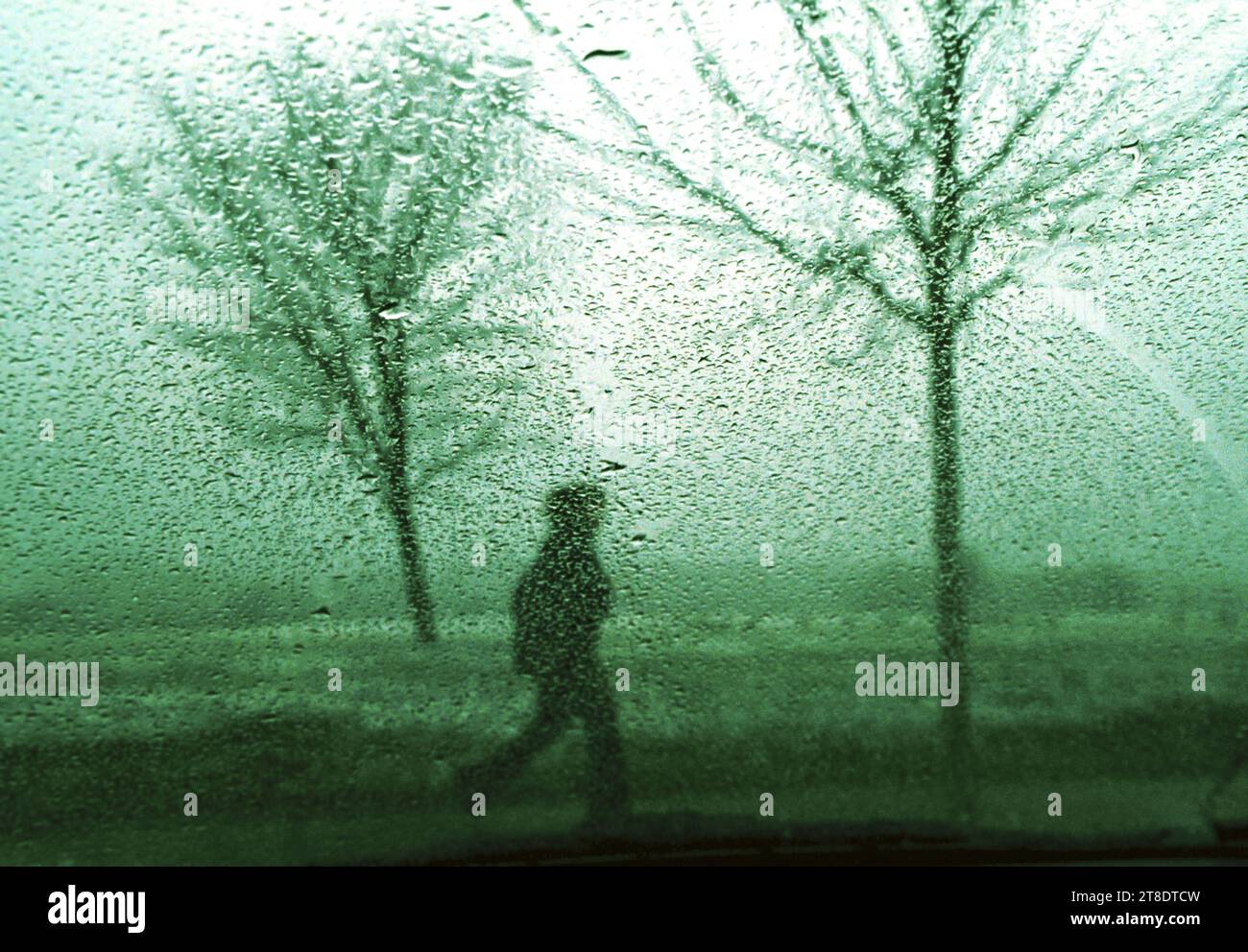 A person running in the rain as seen from a glass window with droplets ...
