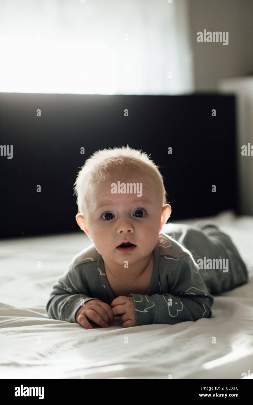Vertical image of baby laying on bed with backlight staring at c Stock ...