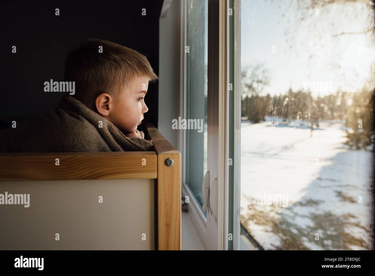 Small boy looks out the window at bright sunny winter day Stock Photo ...