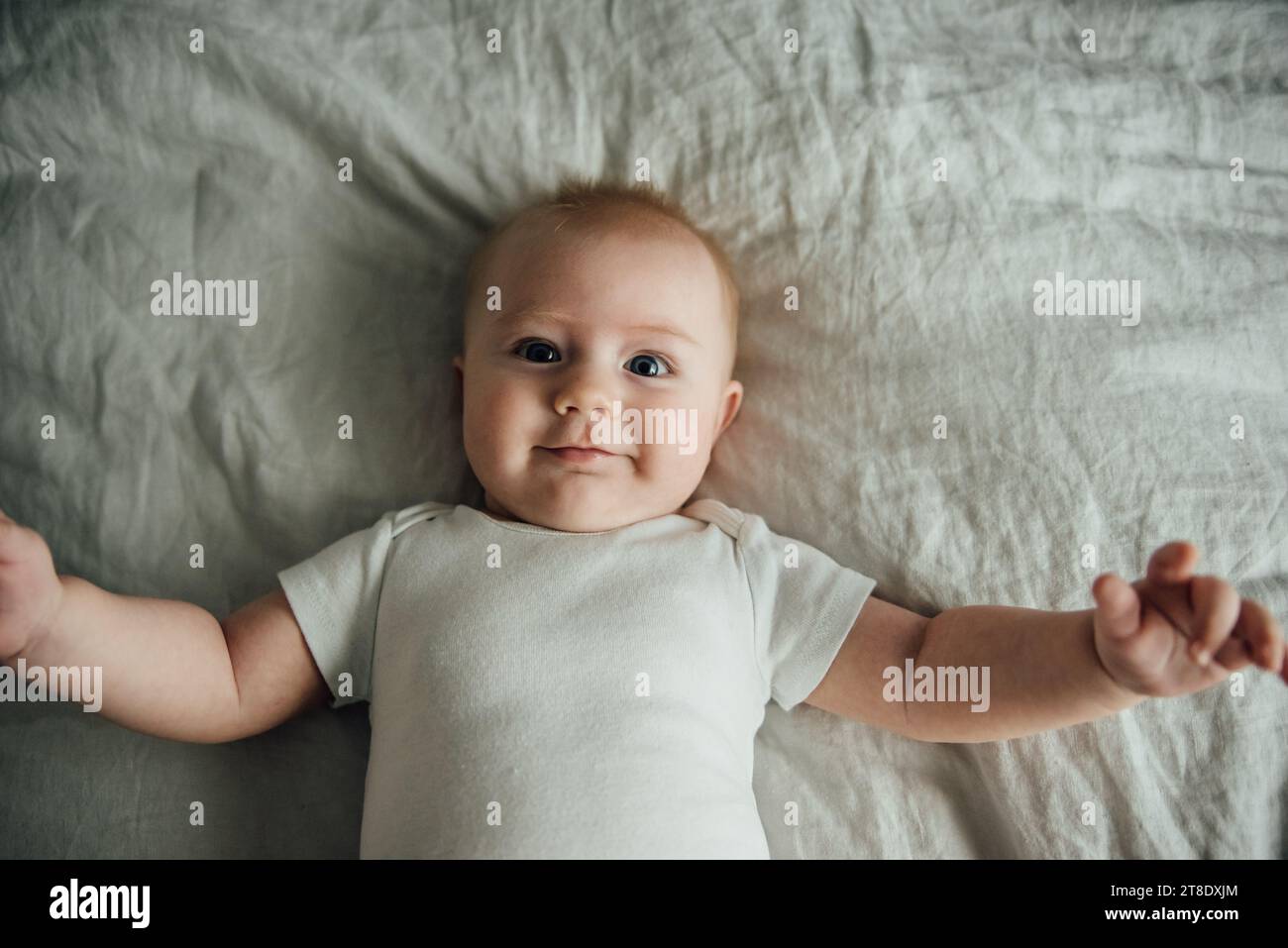 Overhead close up of baby laying on bed and smiling while reachi Stock ...