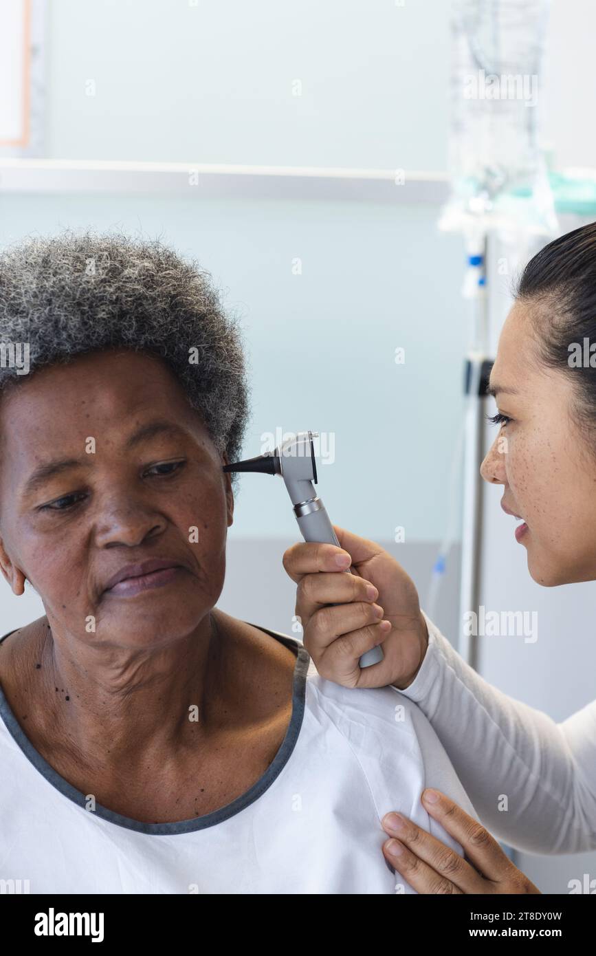 Diverse female doctor testing ear of senior female patient in hospital ...