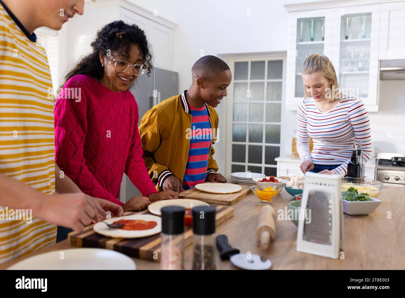 Happy diverse group of teenage friends cooking and making pizza in ...