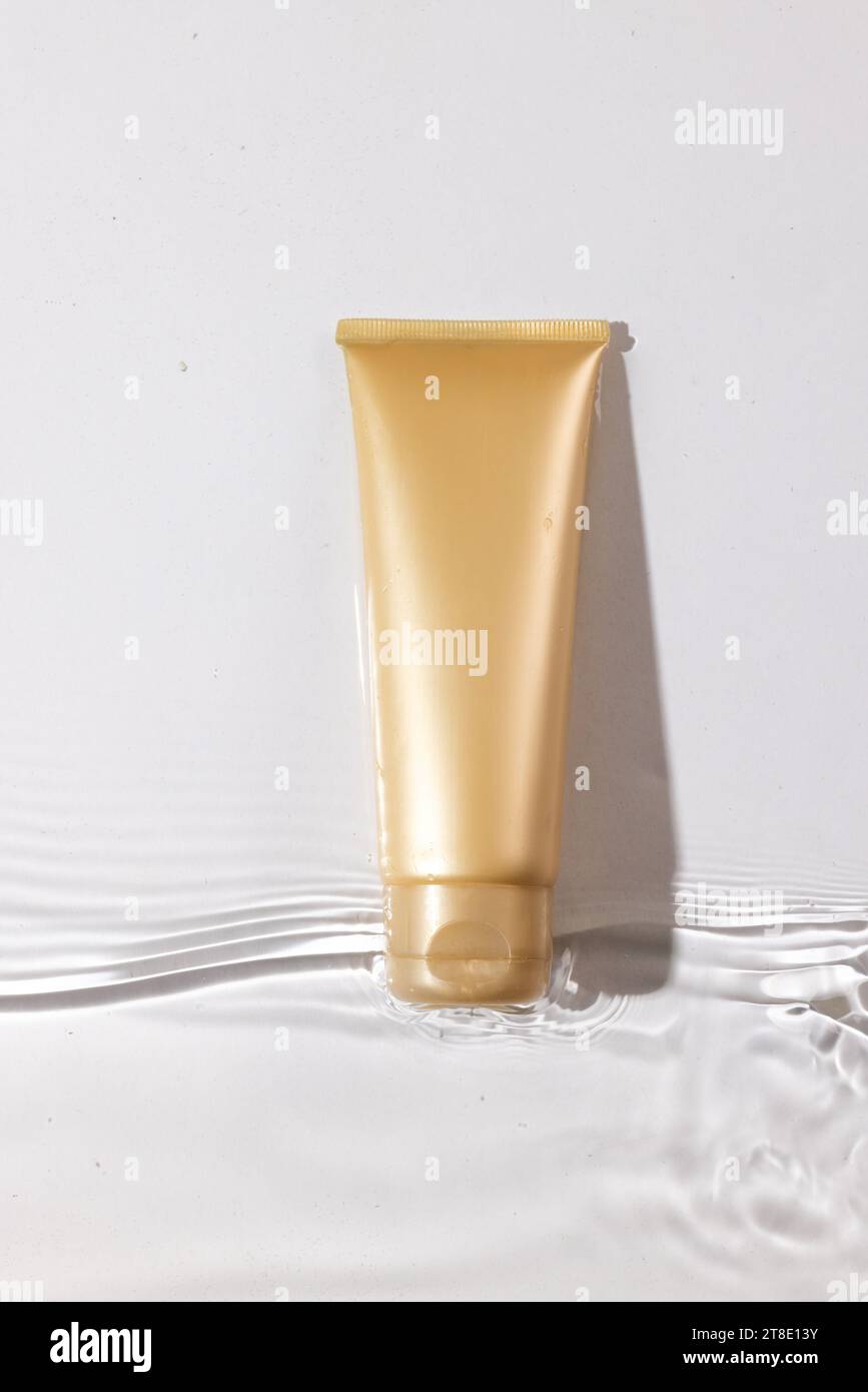 Vertical image of beauty product tube in water with copy space on white ...