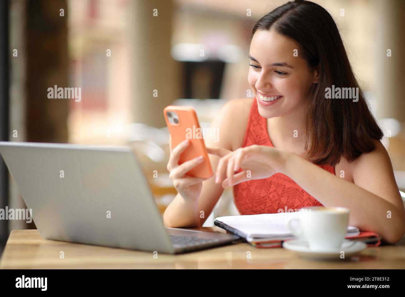 Happy student e-learning with laptop and phone in a coffee shop terrace ...