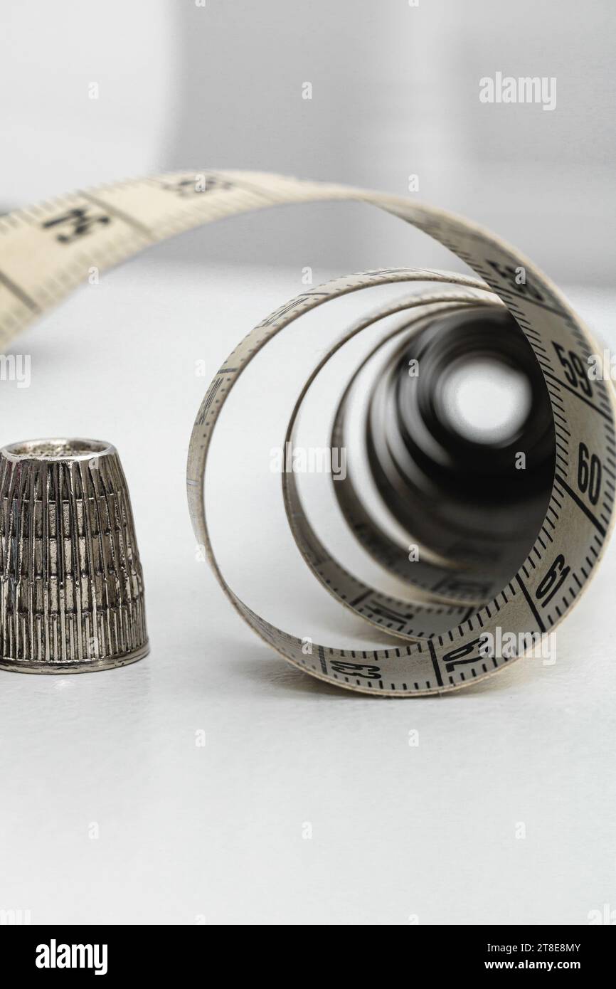 Vertical photo, spiral rolled sewing tape measure and thimble on white ...
