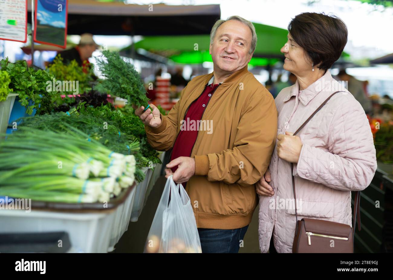 Positive mature male and female picking dill at local grocery bazaar ...