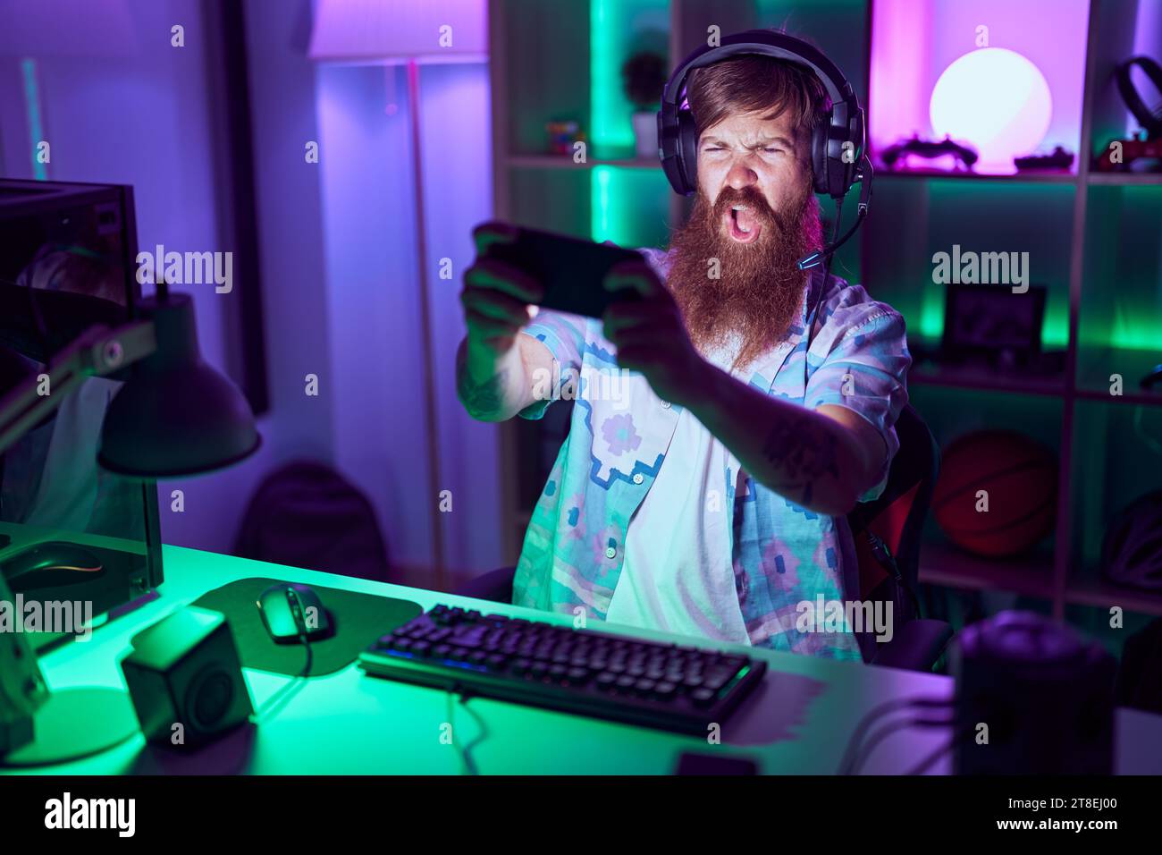 Young redhead man streamer playing video game using smartphone at ...