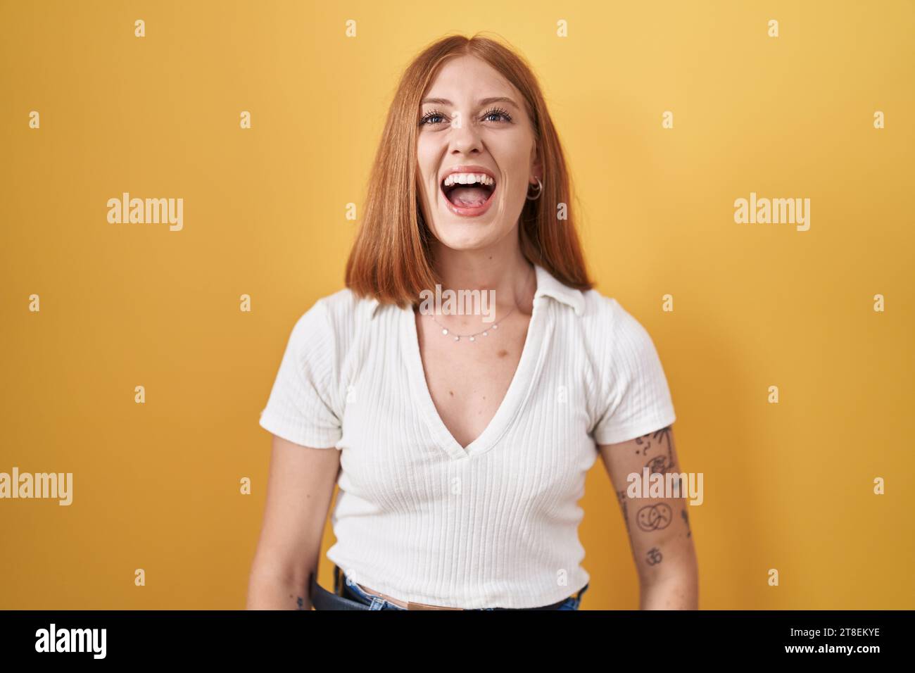 Young redhead woman standing over yellow background angry and mad ...