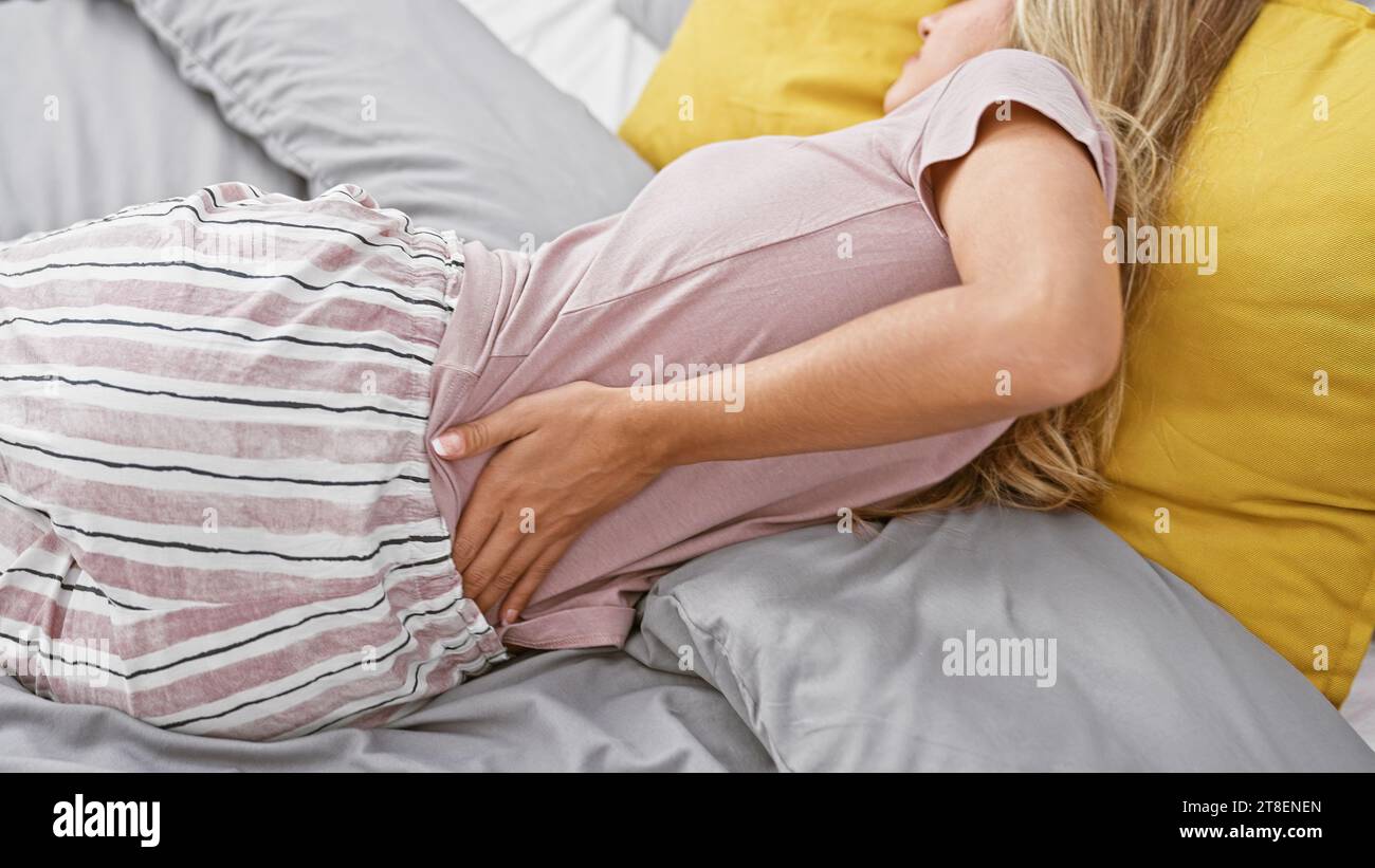 Attractive blonde young woman suffering backache, lying in bed ...