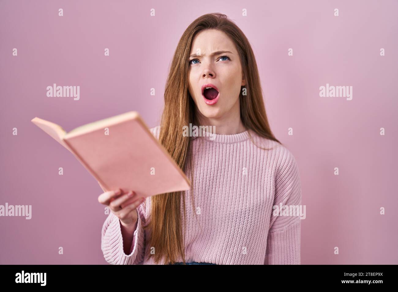 Young caucasian woman reading a book over pink background angry and mad ...