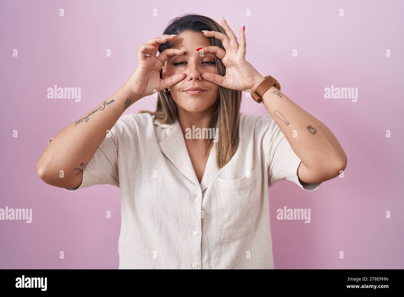 Blonde woman standing over pink background trying to open eyes with ...