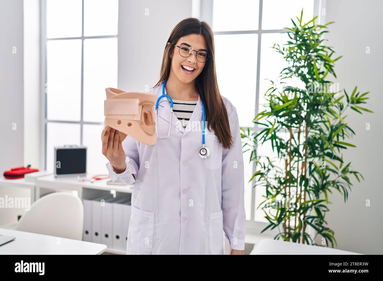 Young brunette doctor woman holding cervical neck collar looking ...