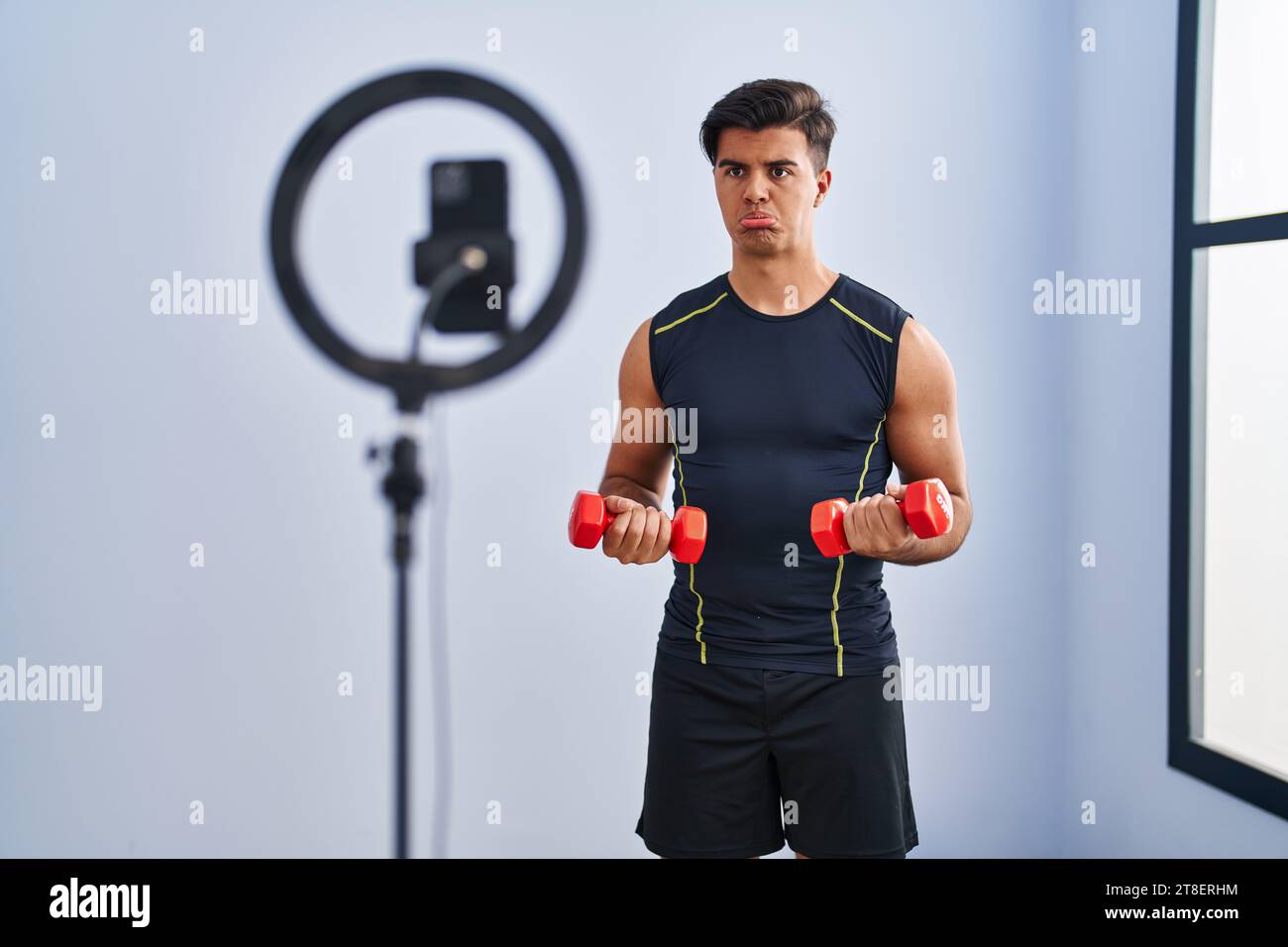 Hispanic man recording training tutorial at the gym depressed and worry ...