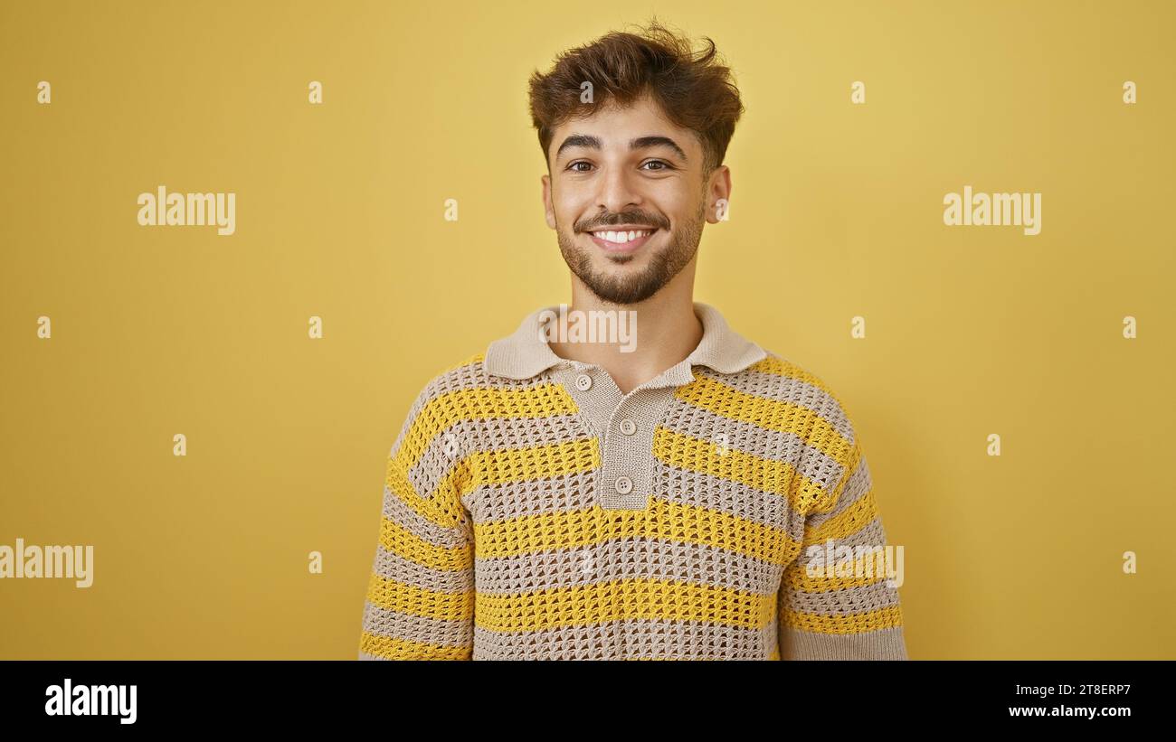 Handsome young arab man, confidently standing, joyfully smiling at wall ...