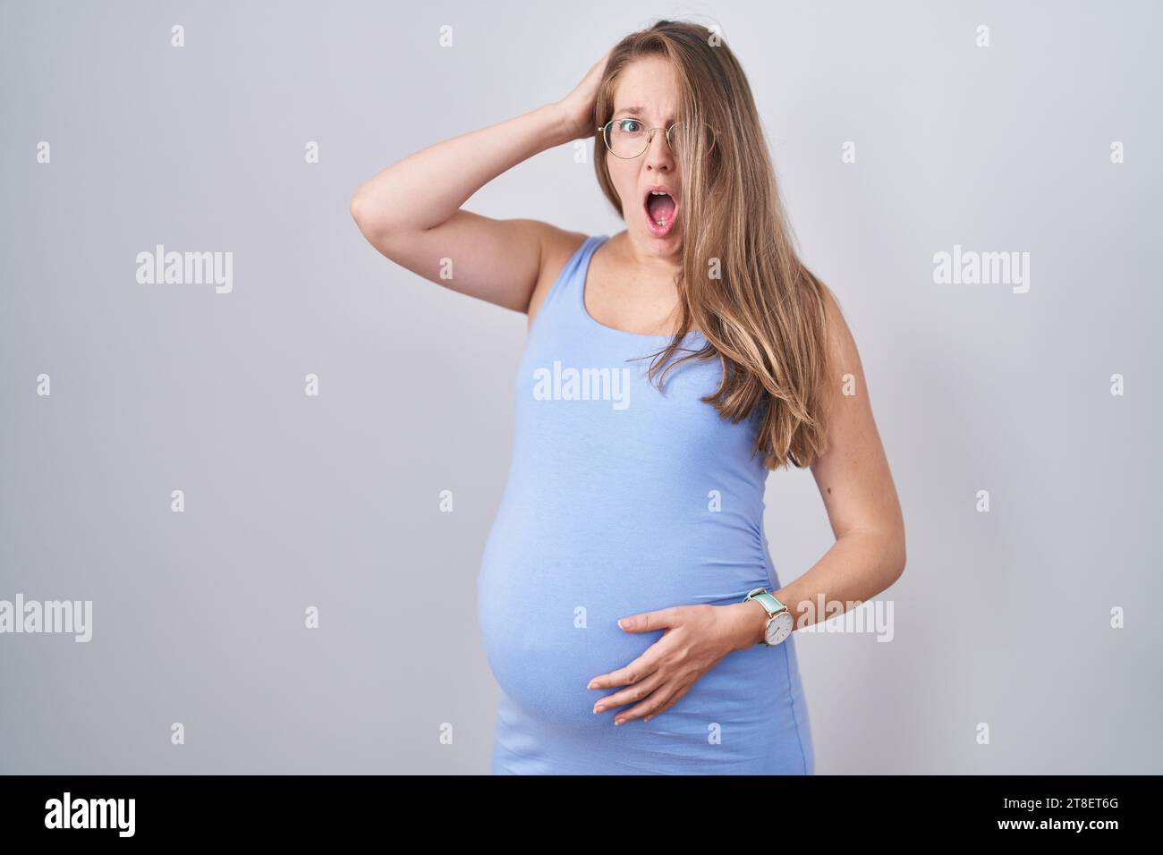 Young pregnant woman standing over white background crazy and scared ...