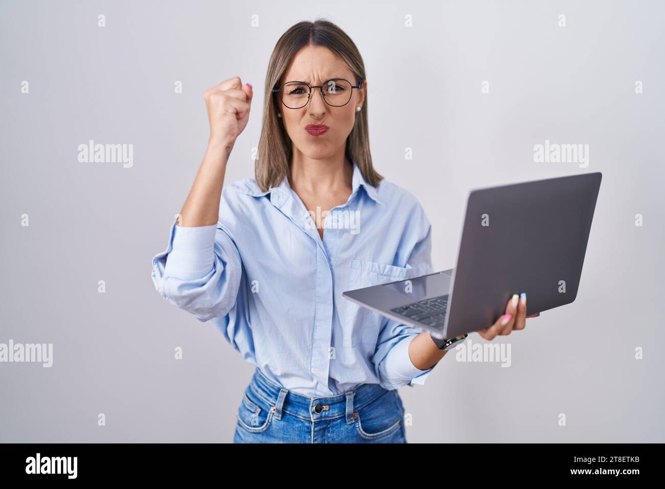 Young woman working using computer laptop angry and mad raising fist ...