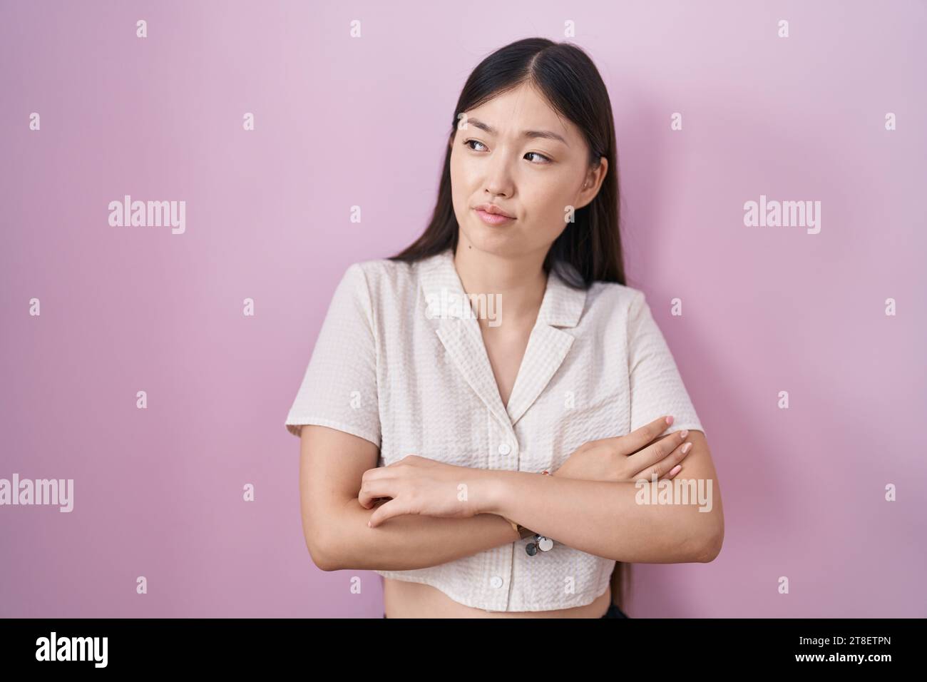 Chinese young woman standing over pink background looking to the side ...