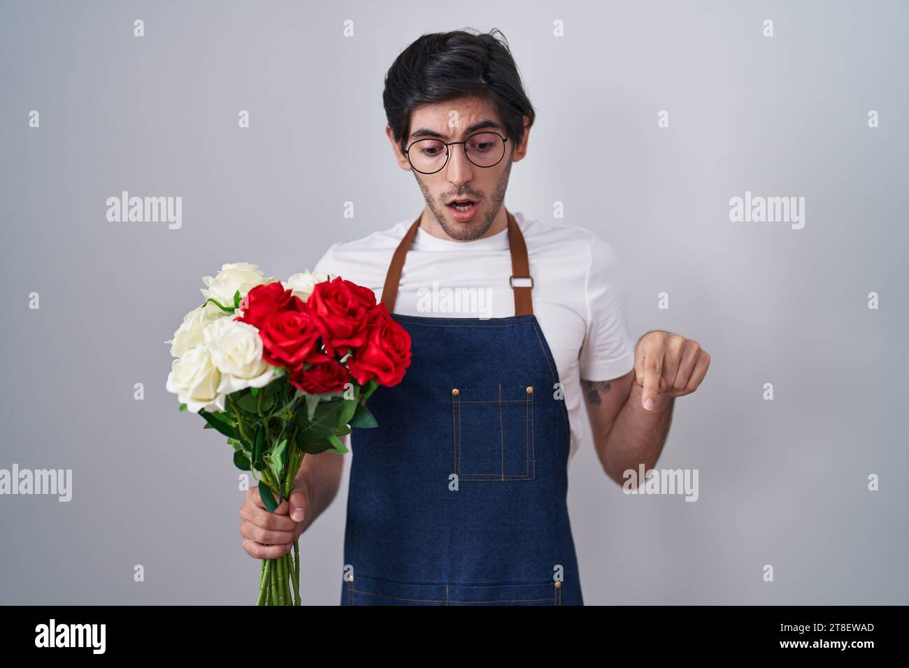 Young hispanic man holding bouquet of white and red roses pointing down ...