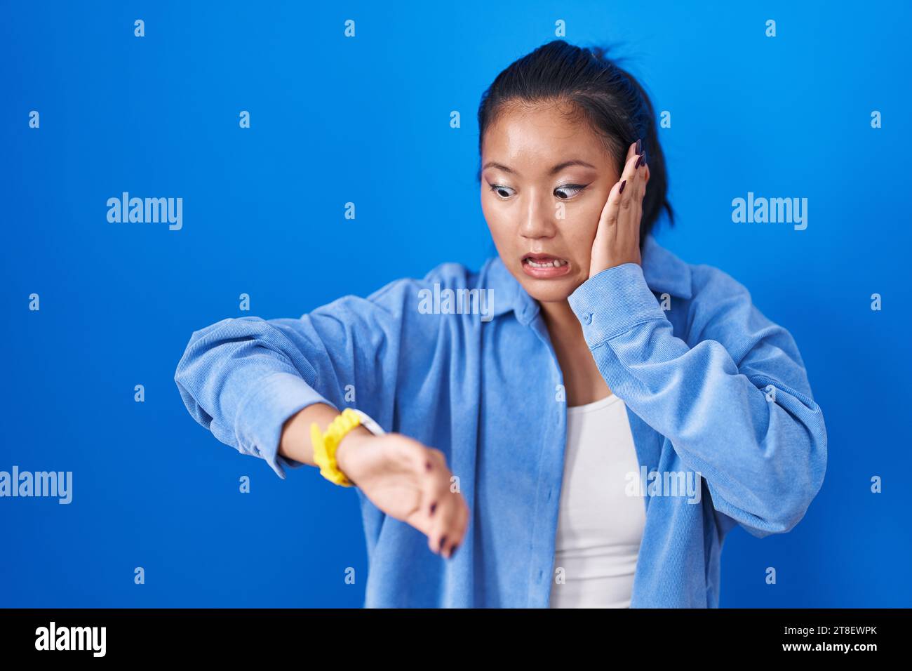 Asian young woman standing over blue background looking at the watch ...