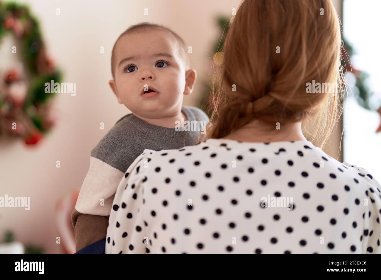Adorable chinese toddler with serious expression on mother arms at home ...