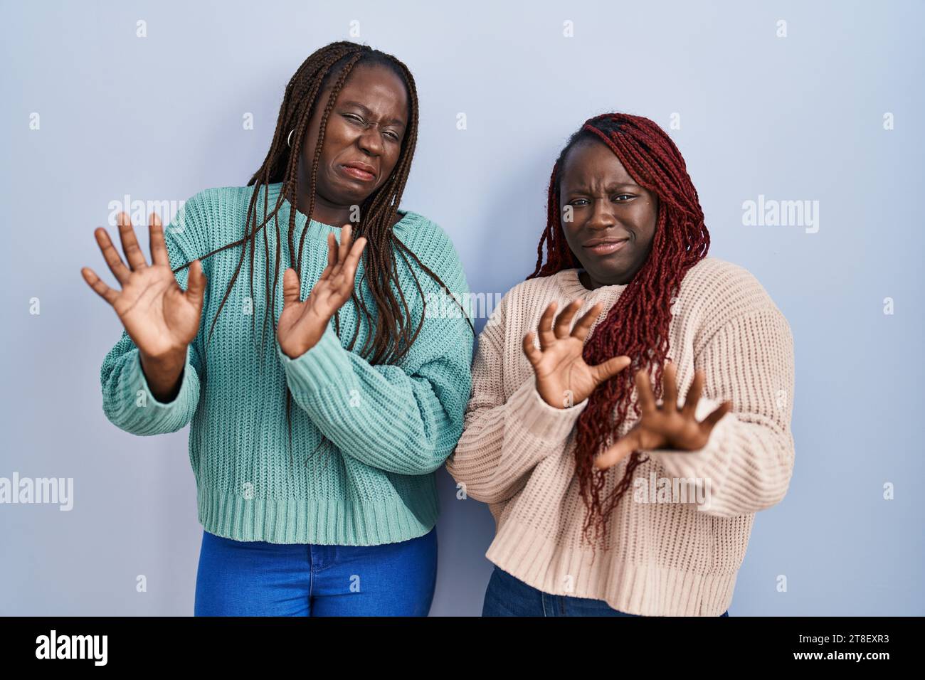 Two african woman standing over blue background disgusted expression ...