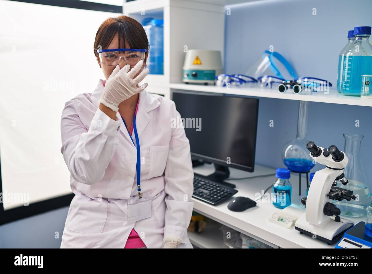 Young brunette woman working at scientist laboratory smelling something ...