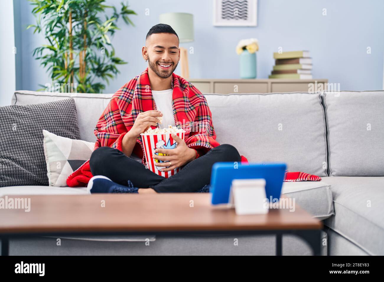 Young hispanic man eating popcorn watching movie on tablet device ...
