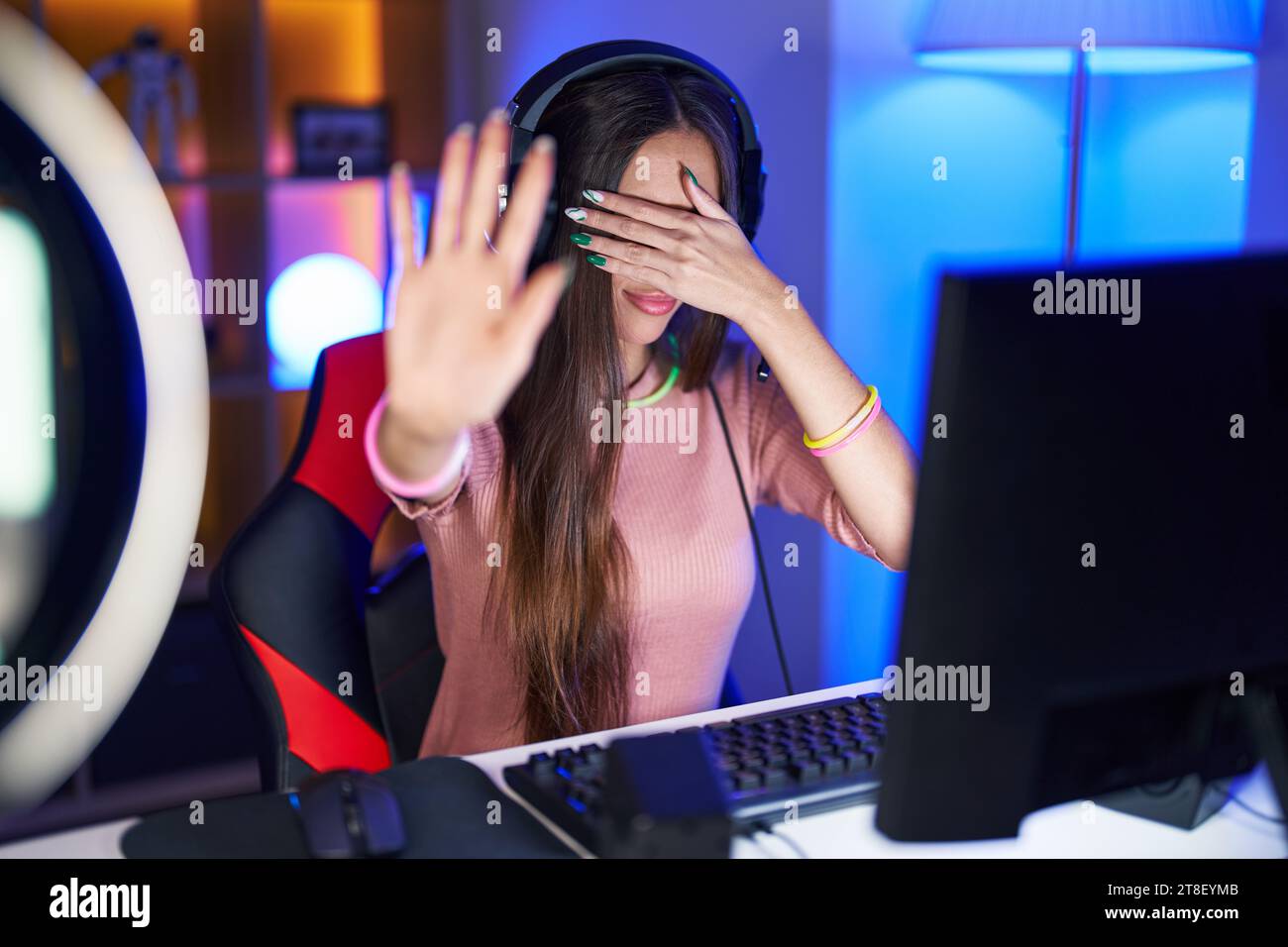 Young hispanic woman playing video games covering eyes with hands and ...