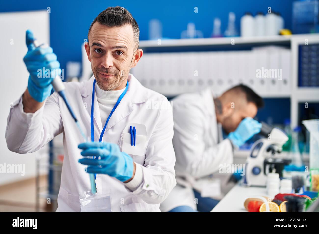 Two men scientists pouring liquid on test tube using microscope at ...