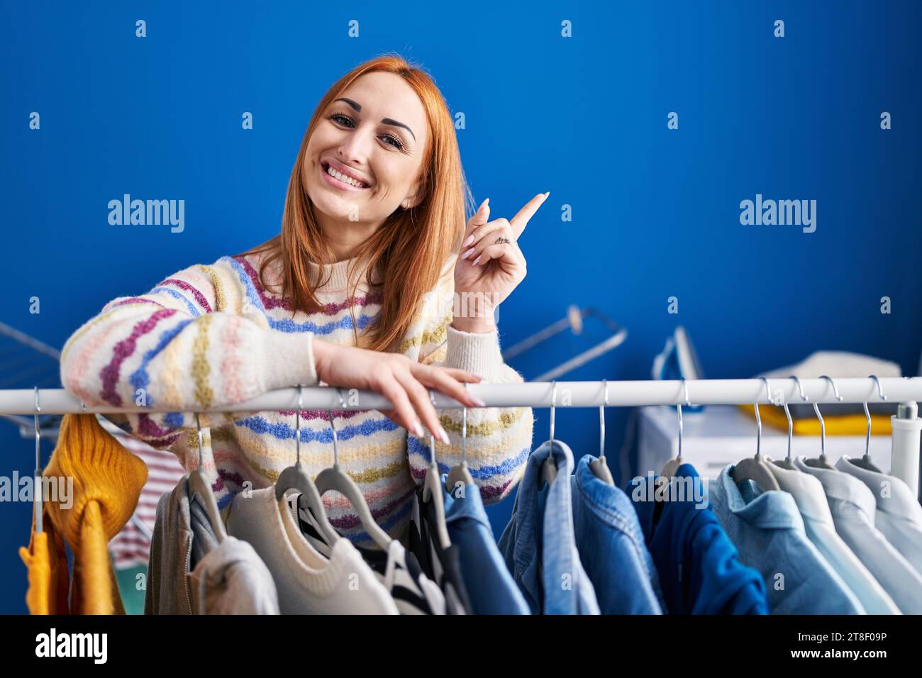 Young woman searching clothes on clothing rack smiling happy pointing ...
