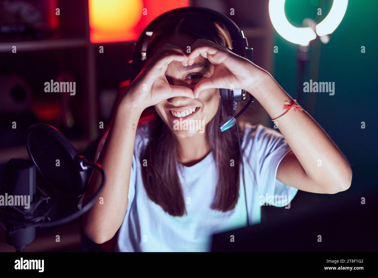 Young beautiful hispanic woman streamer smiling confident doing heart ...